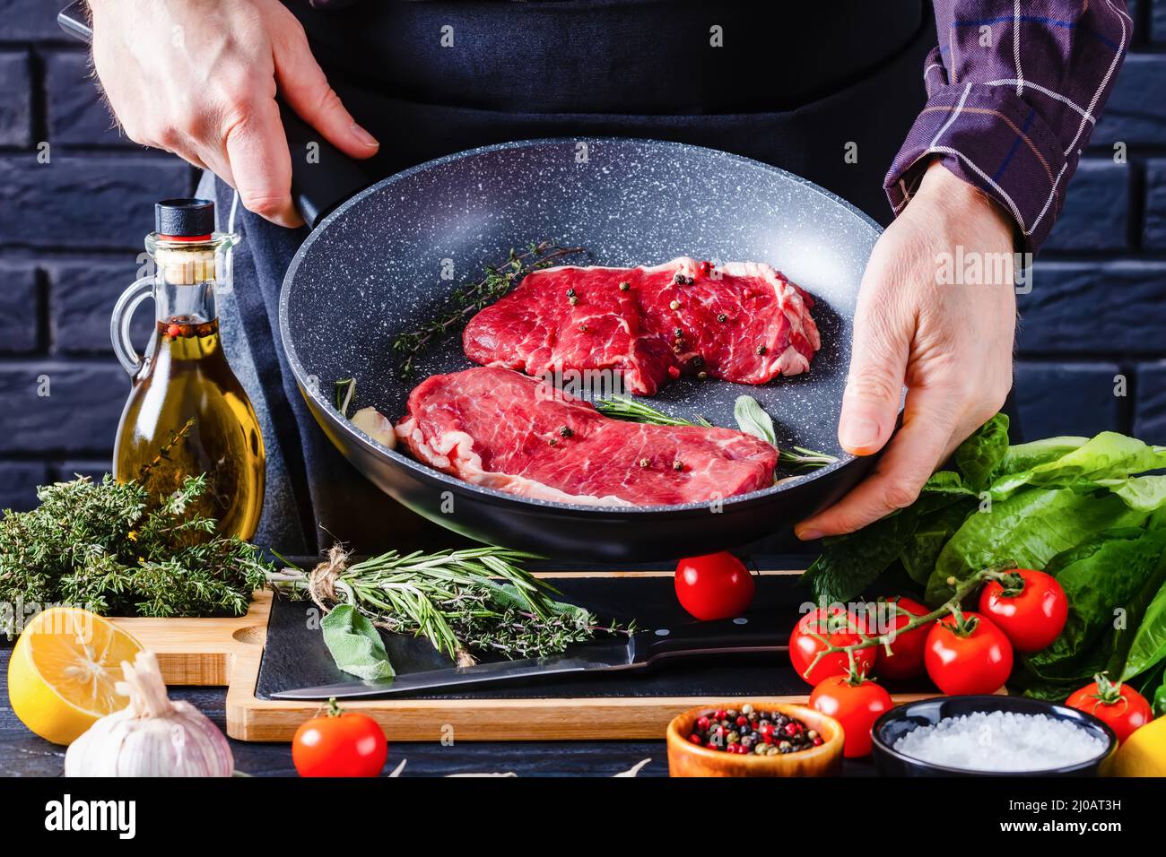 male chef is holding frying pan with raw beef steaks, horizontal view ...
