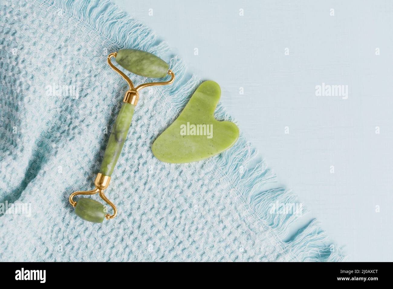 Green jade face roller and gua sha scraper on light blue background ...