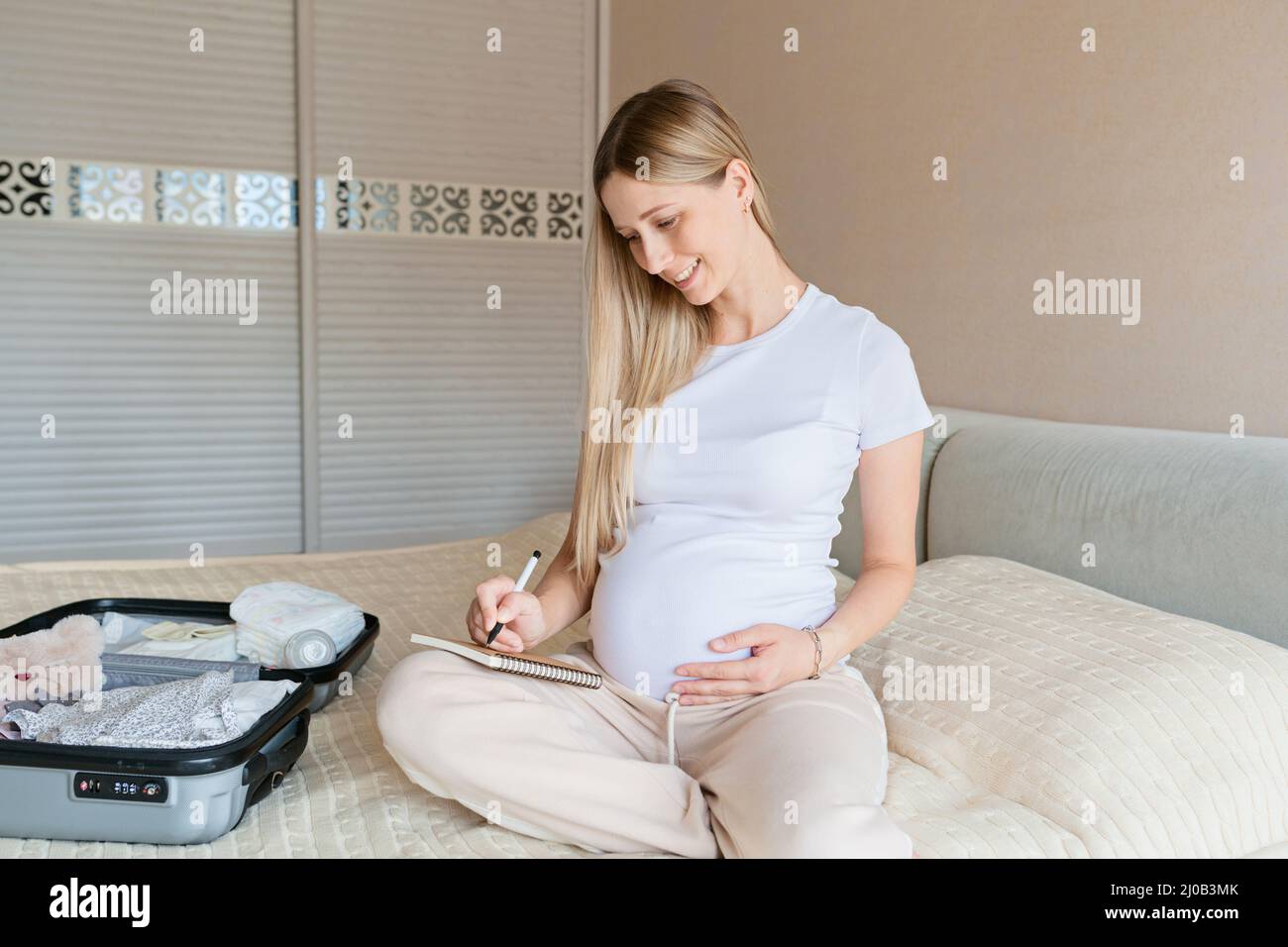 Young Pregnant woman packing suitcase for maternity hospital at home ...