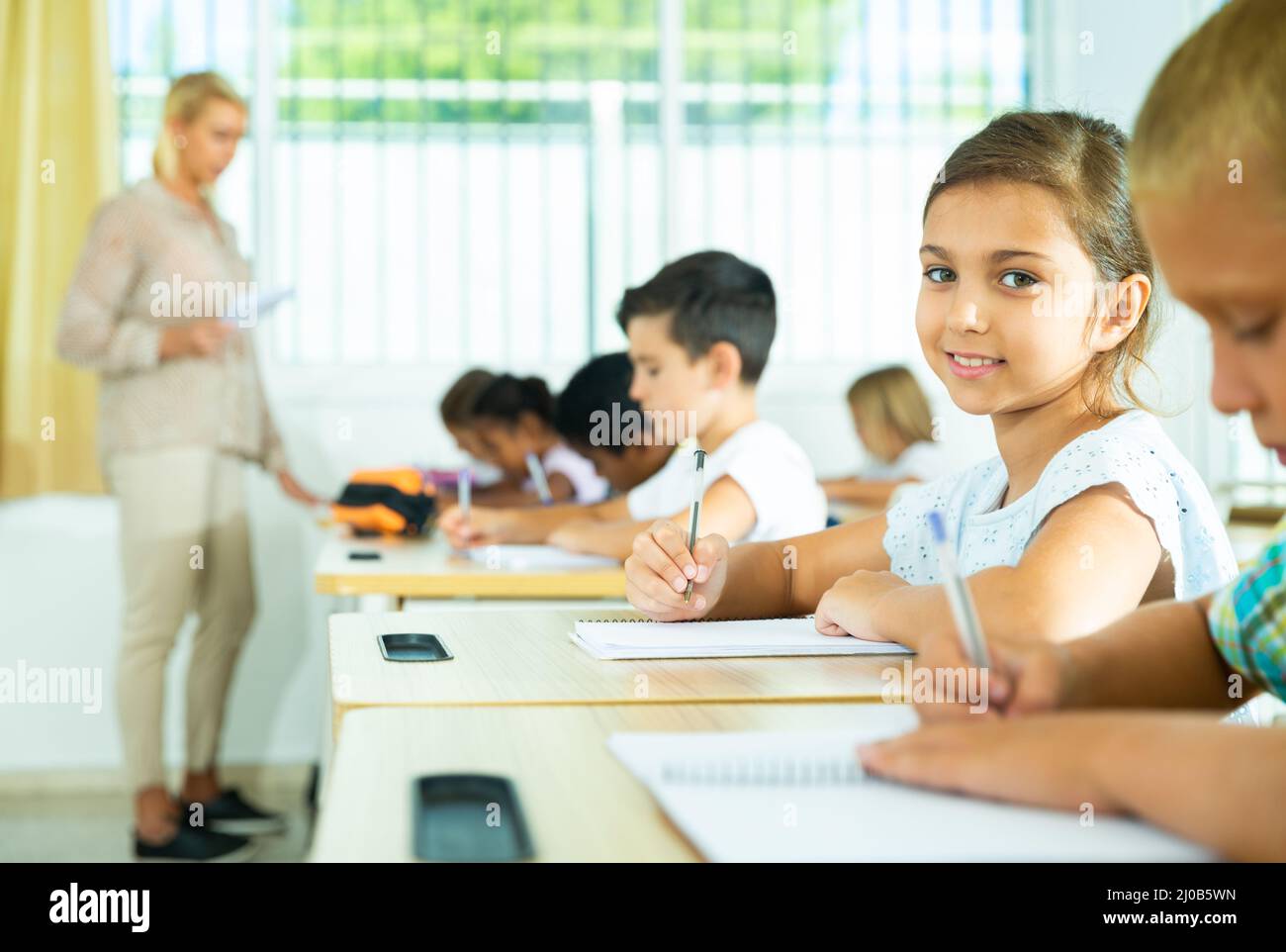 Side view of group of primary school students and positive girl at desk ...