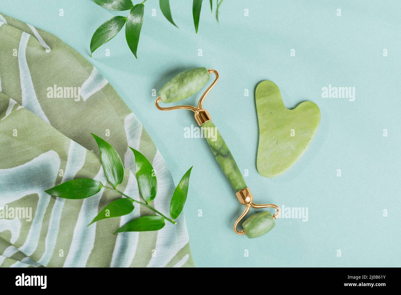 Top view of Green jade face roller and gua sha scraper with leaves on ...