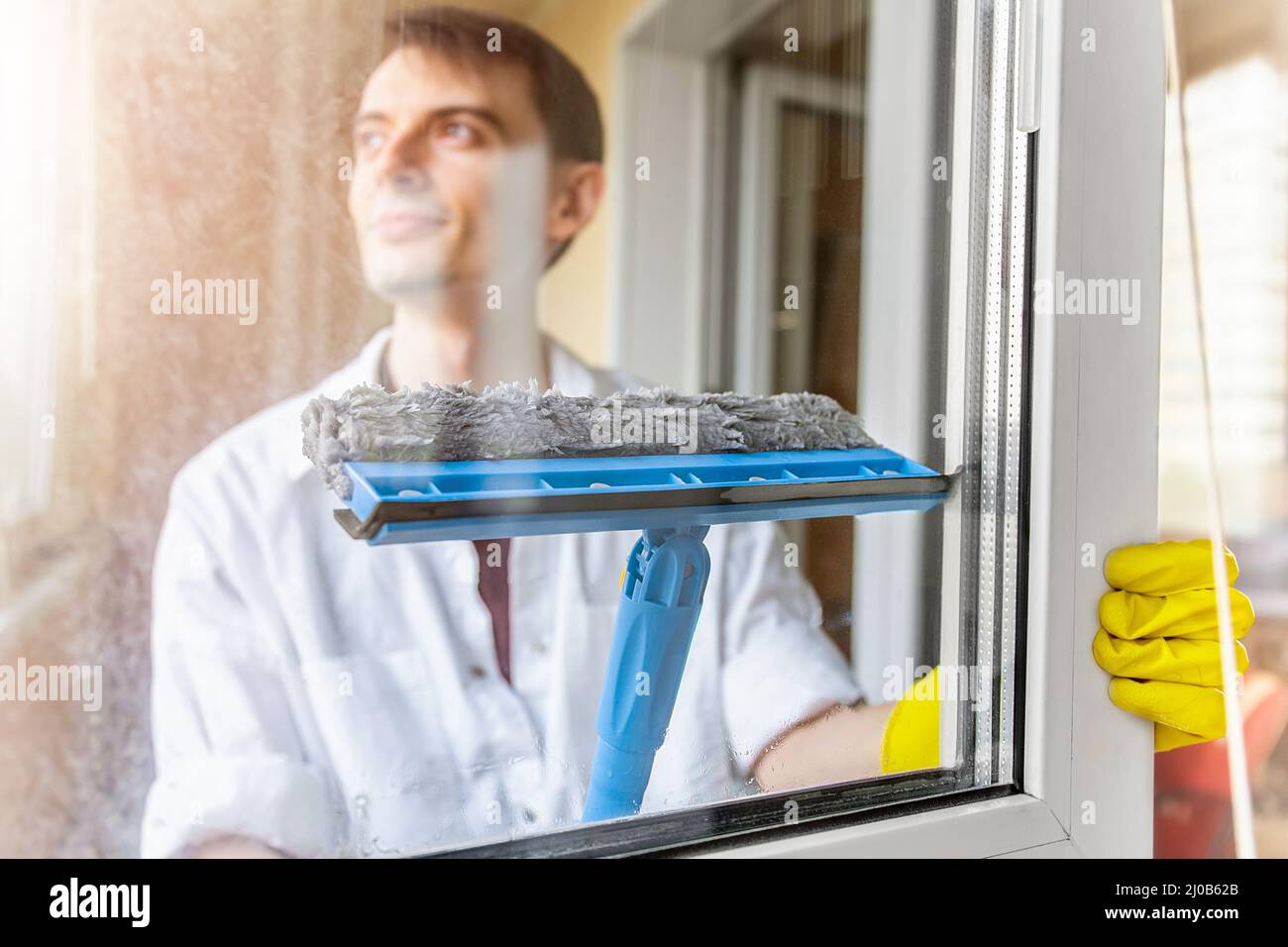 Cleaning concept. Smiling young man washing window in yellow gloves ...