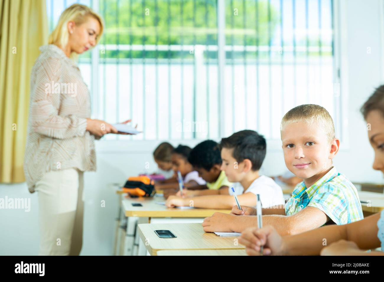 Boys sits at a desk next to diligent elementary school students Stock ...