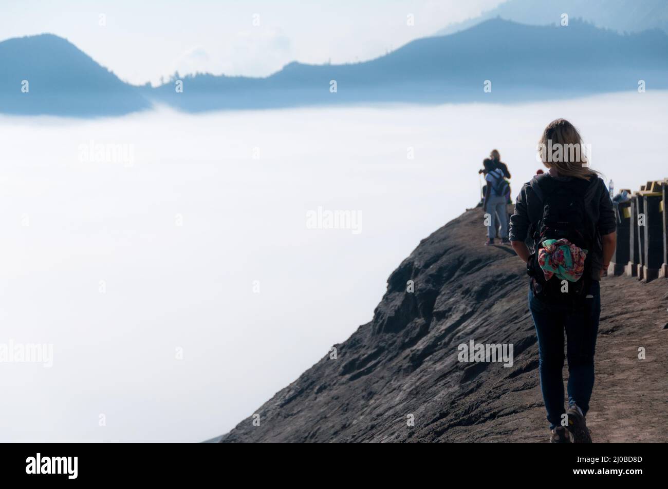 Woman walking along top of volcano next to fog and mist Stock Photo - Alamy