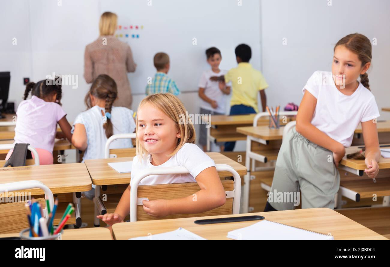 Positive primary school students are talking about homework at desk ...