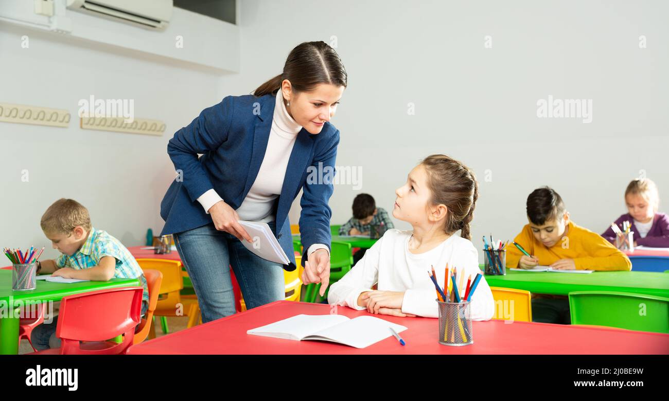Friendly teacher woman helping girl during lesson in schoolroom Stock ...
