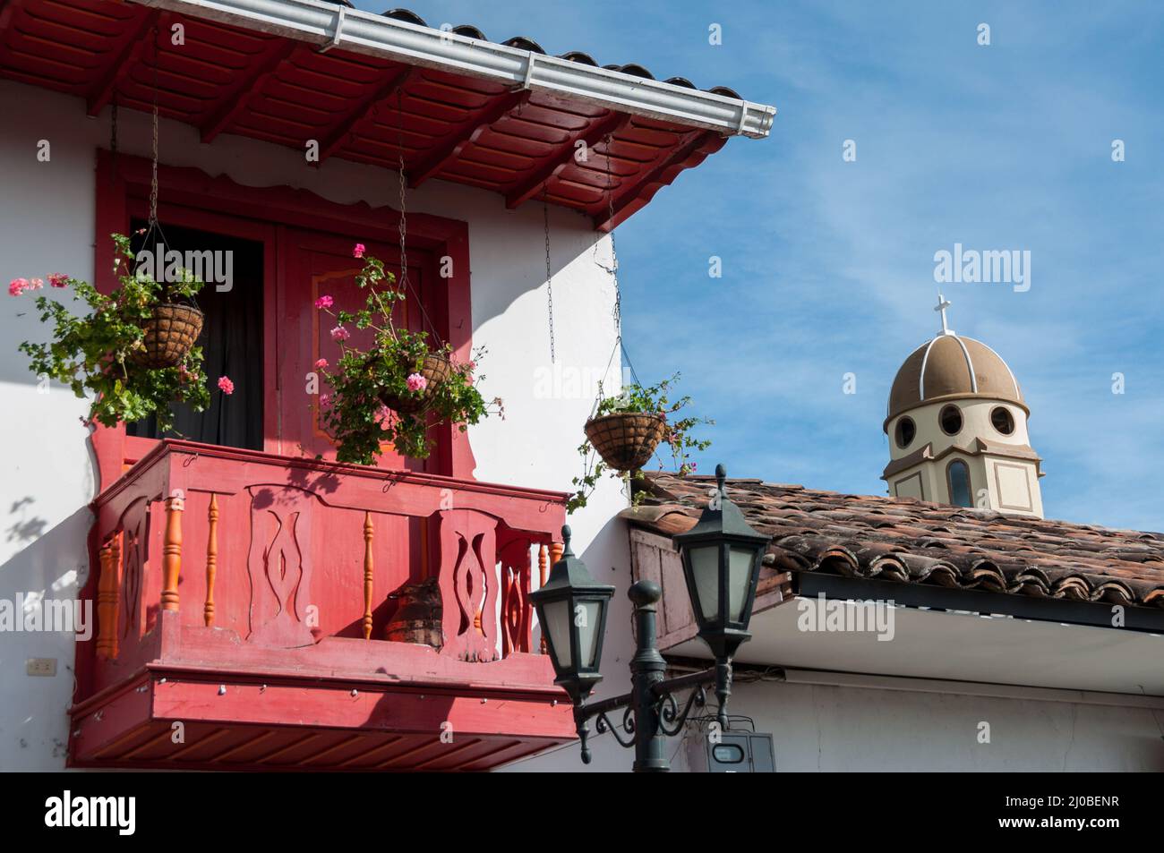 Red balcony and the tower of a church in background under blue sky ...