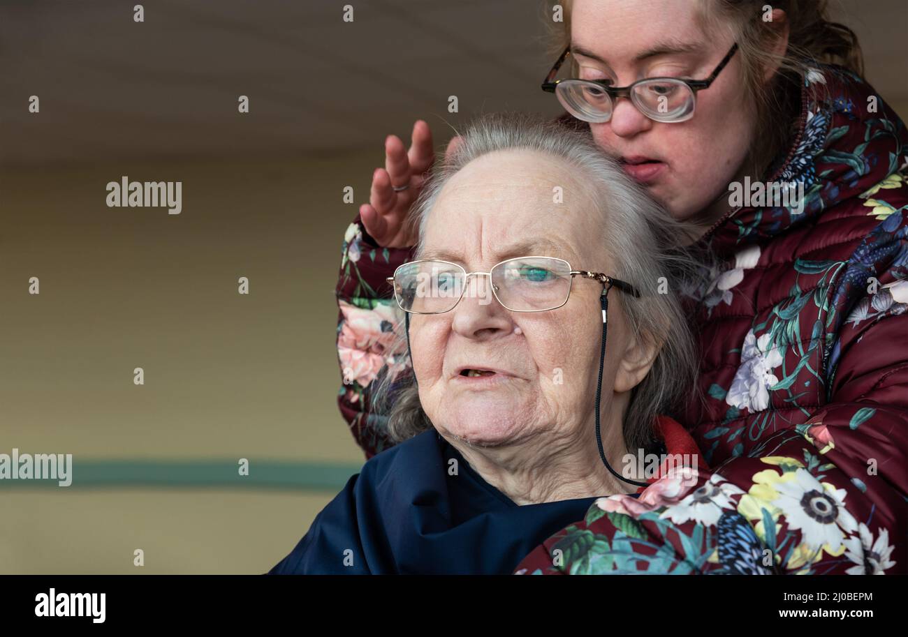 Daughter with Down Syndrome holding her senior mother, sitting in a ...