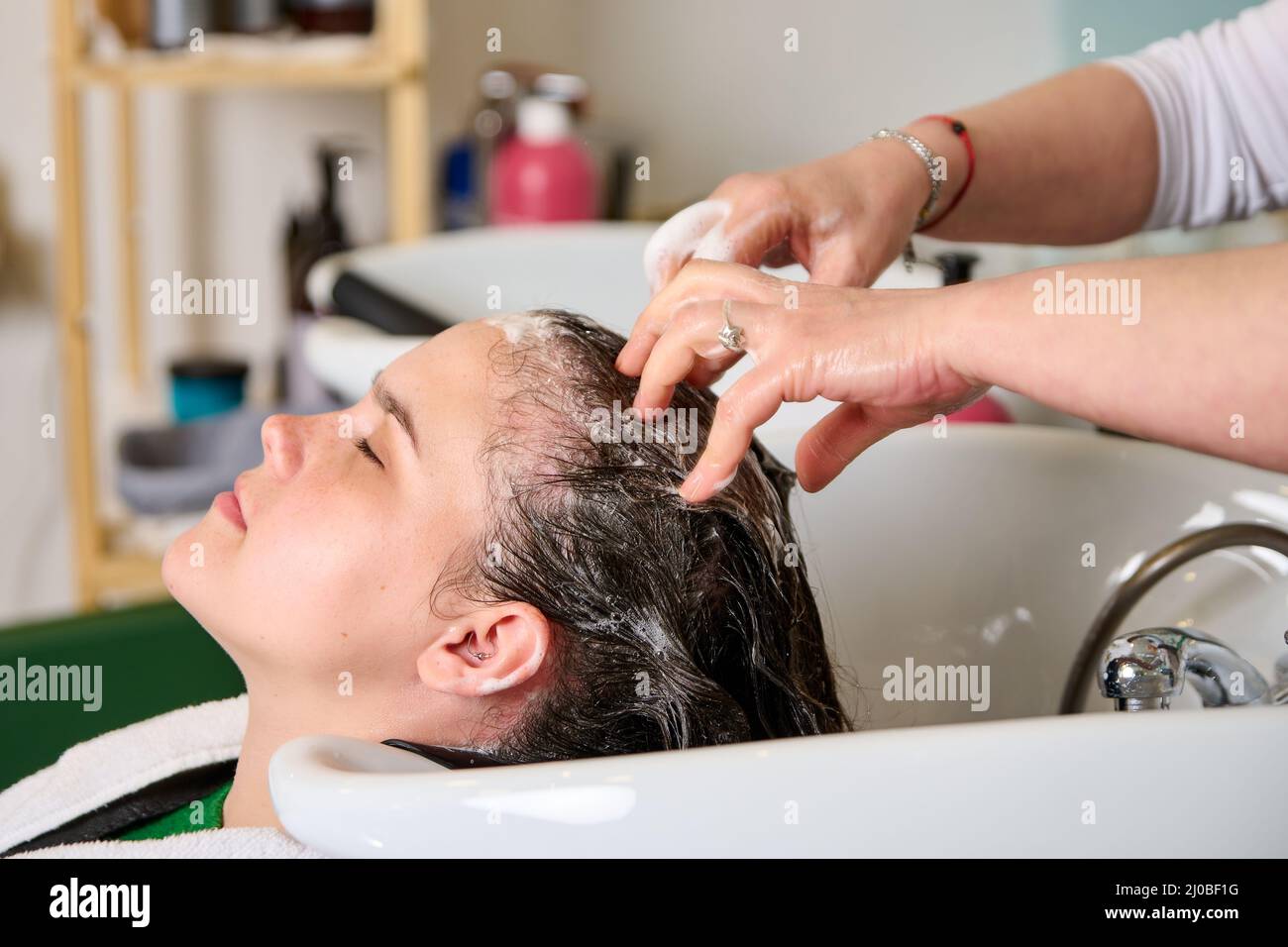 A woman in a hairdresser salon and the barber putting shampoo on her ...