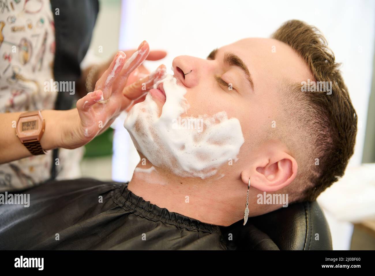 A man in a hairdresser salon and the barber putting a shaving foam on ...