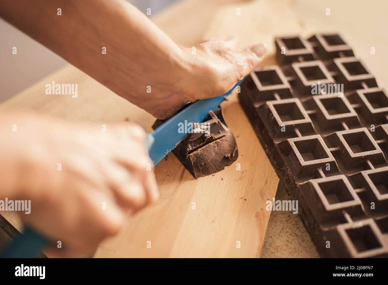 Close up of a woman hands chopping chocolate block for celebratory cake ...