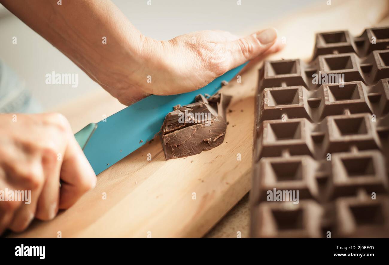 Close up of a woman hands chopping chocolate block for celebratory cake ...