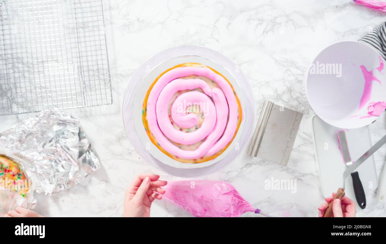 Flat lay. Step by step. Frosting round funfetti cake layers with pink ...