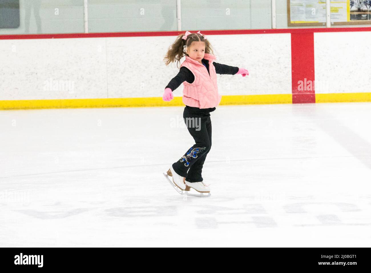 Little girl practicing figure skating moves on the indoor ice rink ...