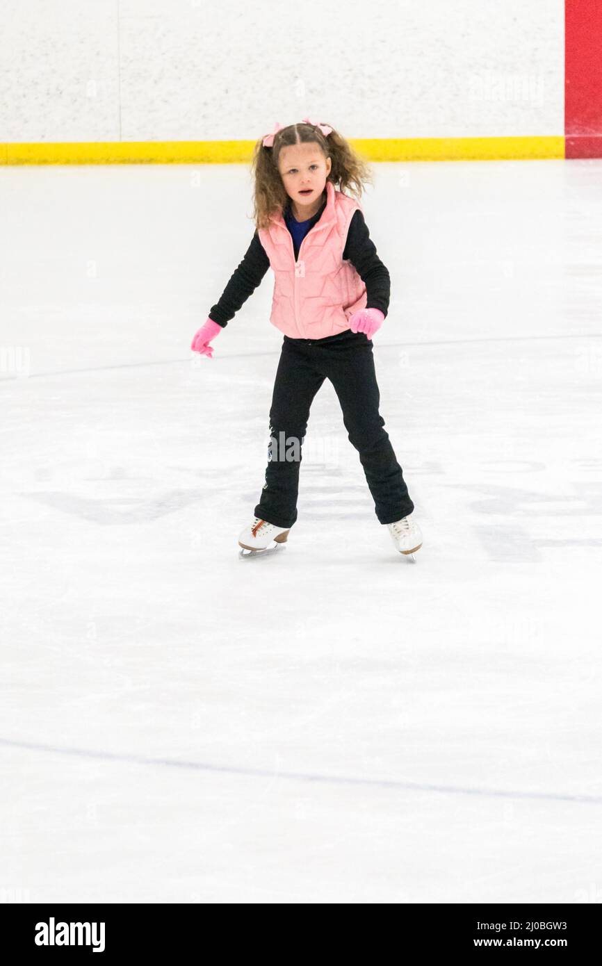 Little girl practicing figure skating moves on the indoor ice rink ...