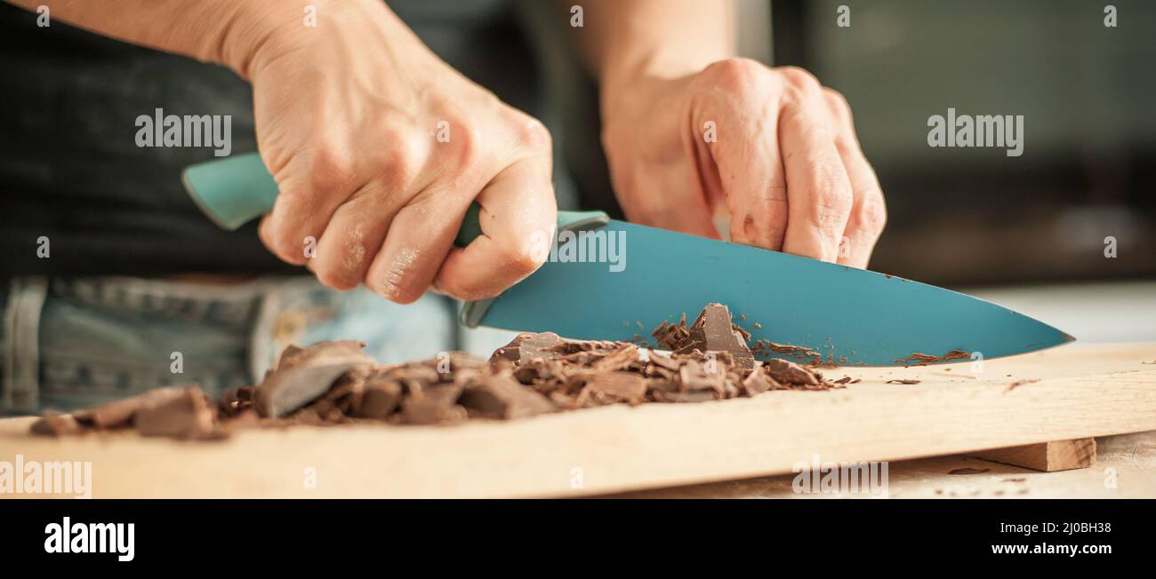 Close up of a woman hands chopping chocolate block for celebratory cake ...
