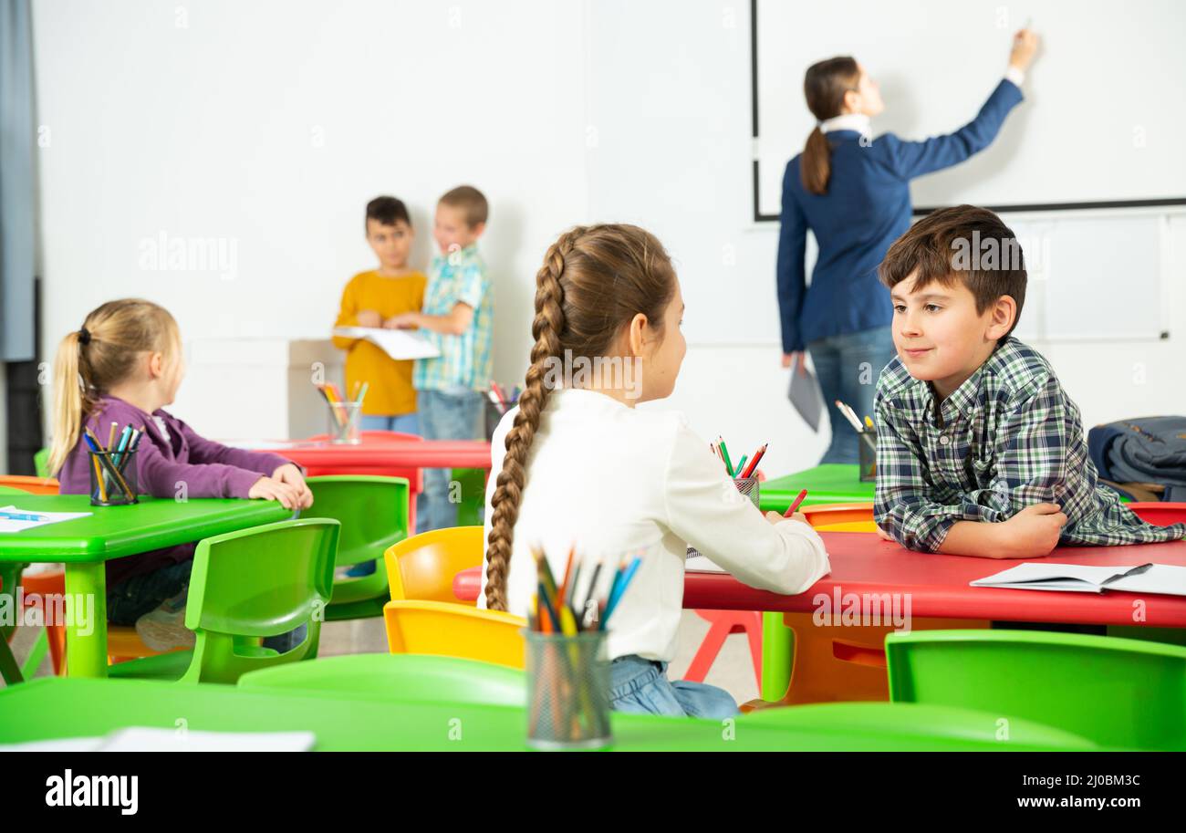 Portrait of schoolchildren sitting in classroom and chatting during ...