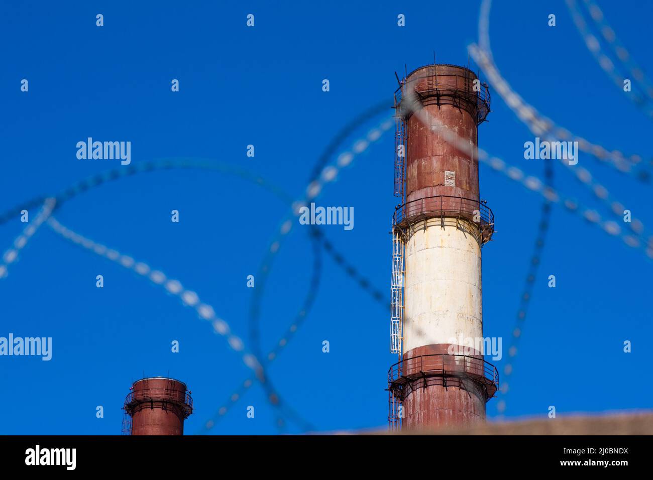 Barbed wire and pipe enterprises on the background of blue sky. Russia ...
