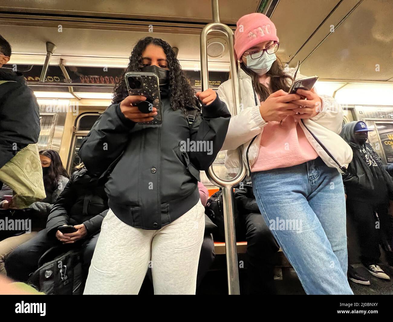 Two young female subway train riders glued to their phones as they ride ...