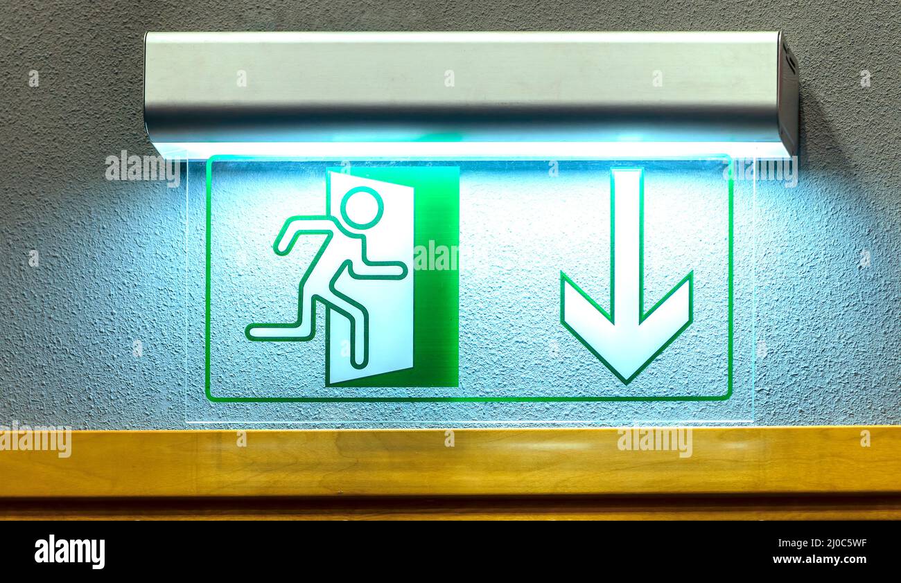 Illuminated green emergency exit light sign on the wall. Close up Stock ...