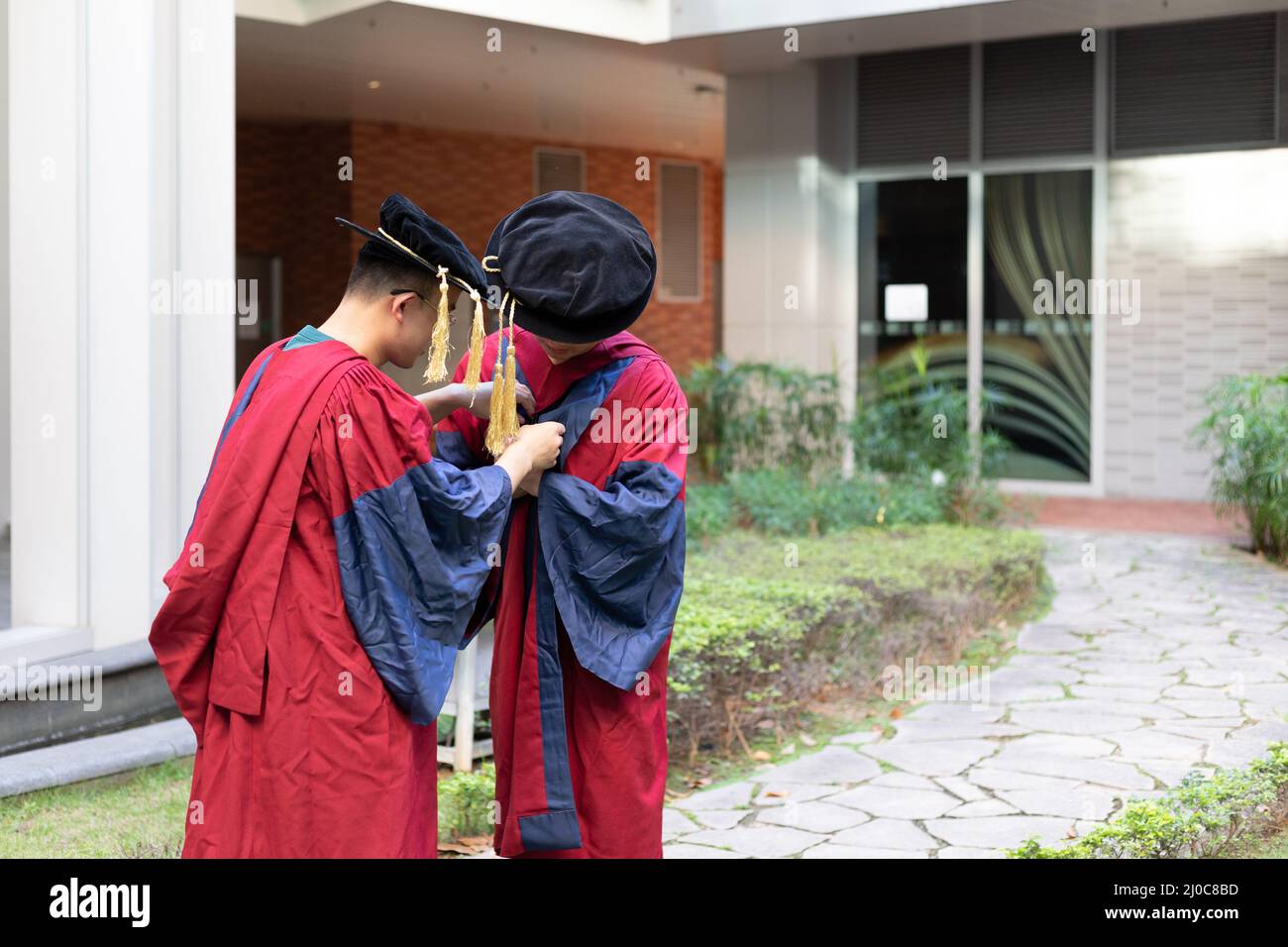 two happy proud PhD graduated male students help each other to put on ...