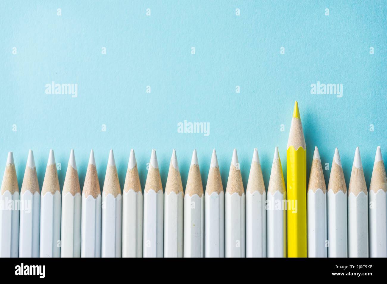 Business concept - lot of white pencils and one color pencil on blue ...