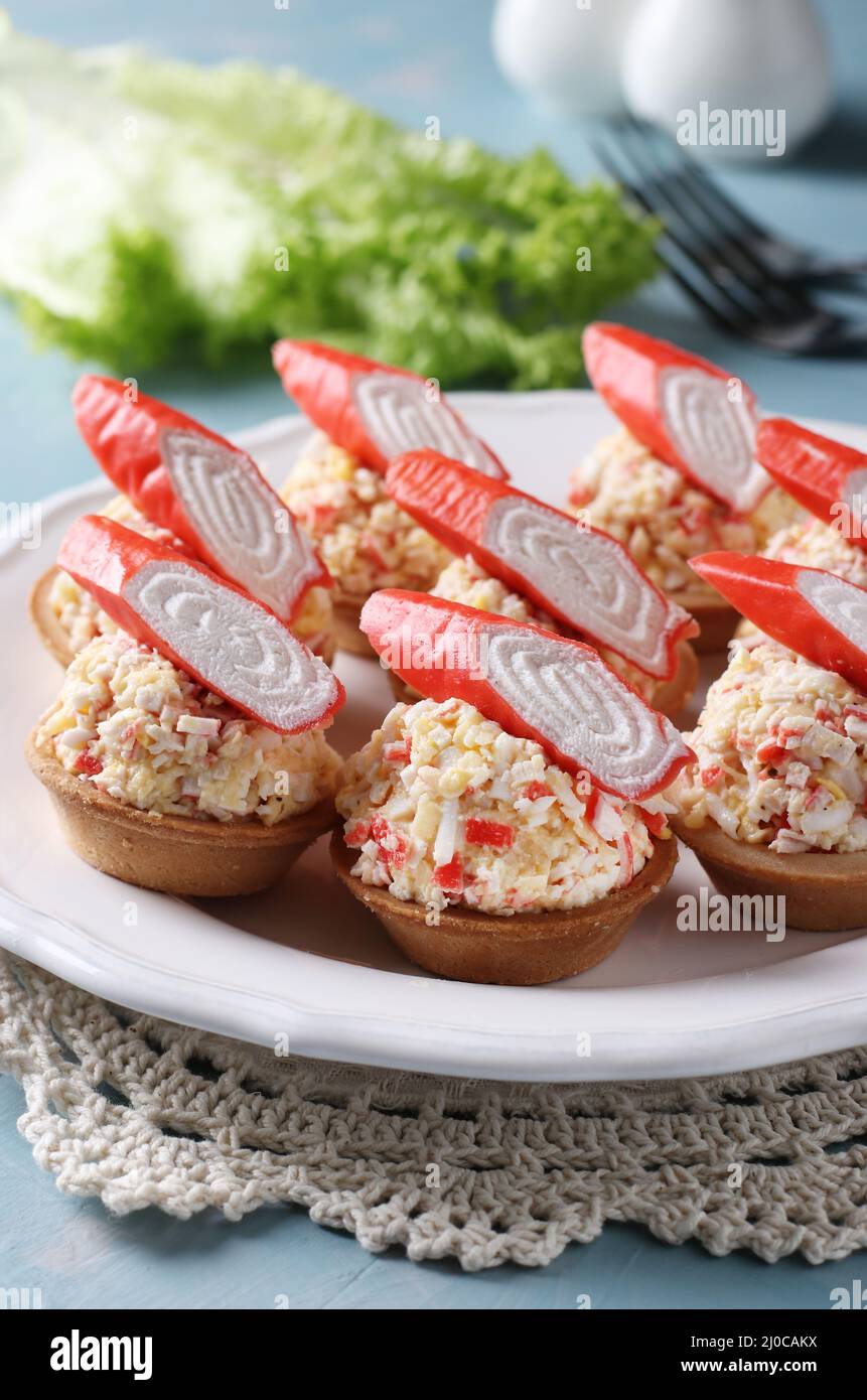 Tartlets with crab sticks, eggs, cheese and cucumber on a plate on blue ...