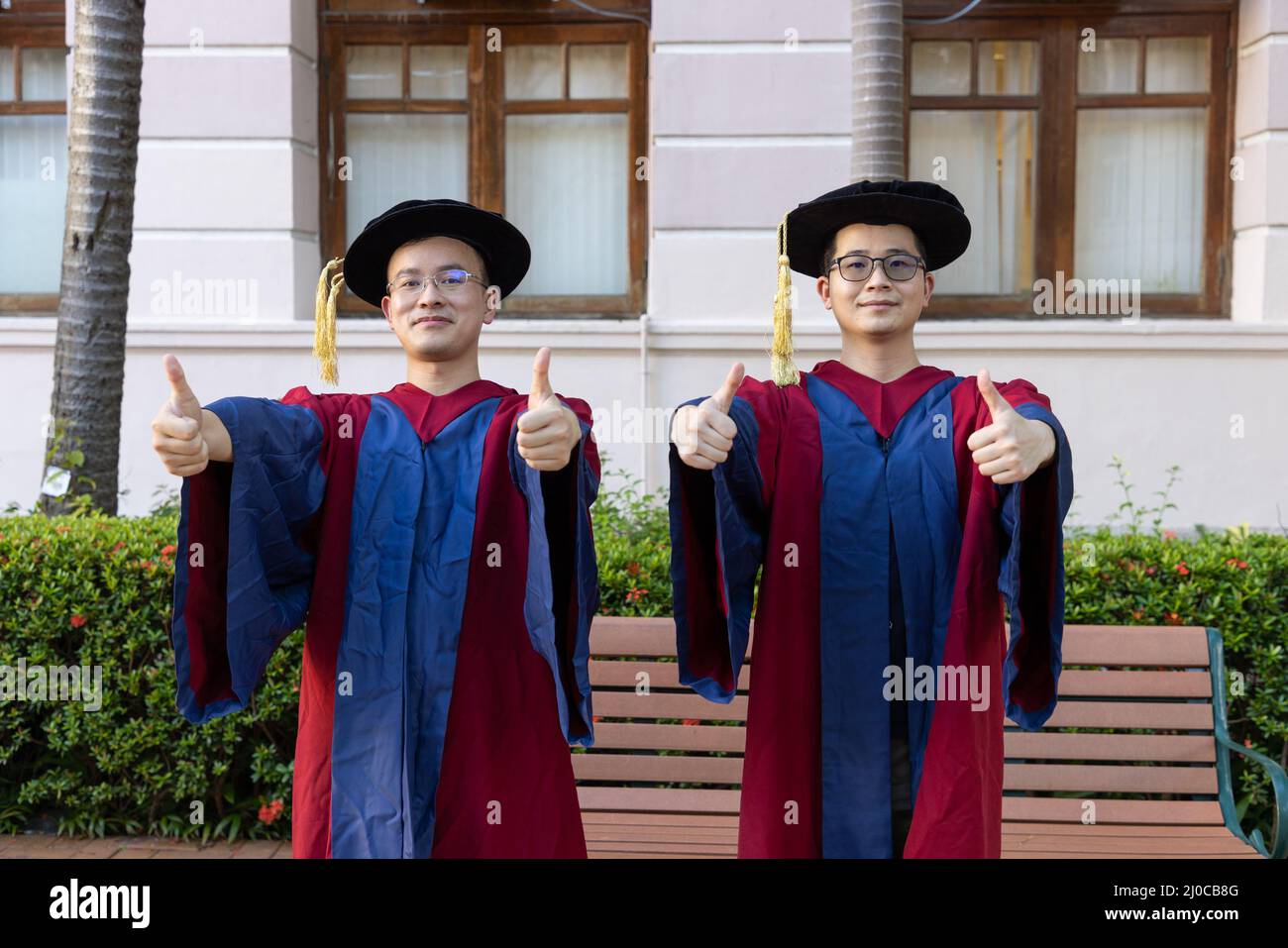 two happy proud PhD graduated male students in Academic dress gown show ...