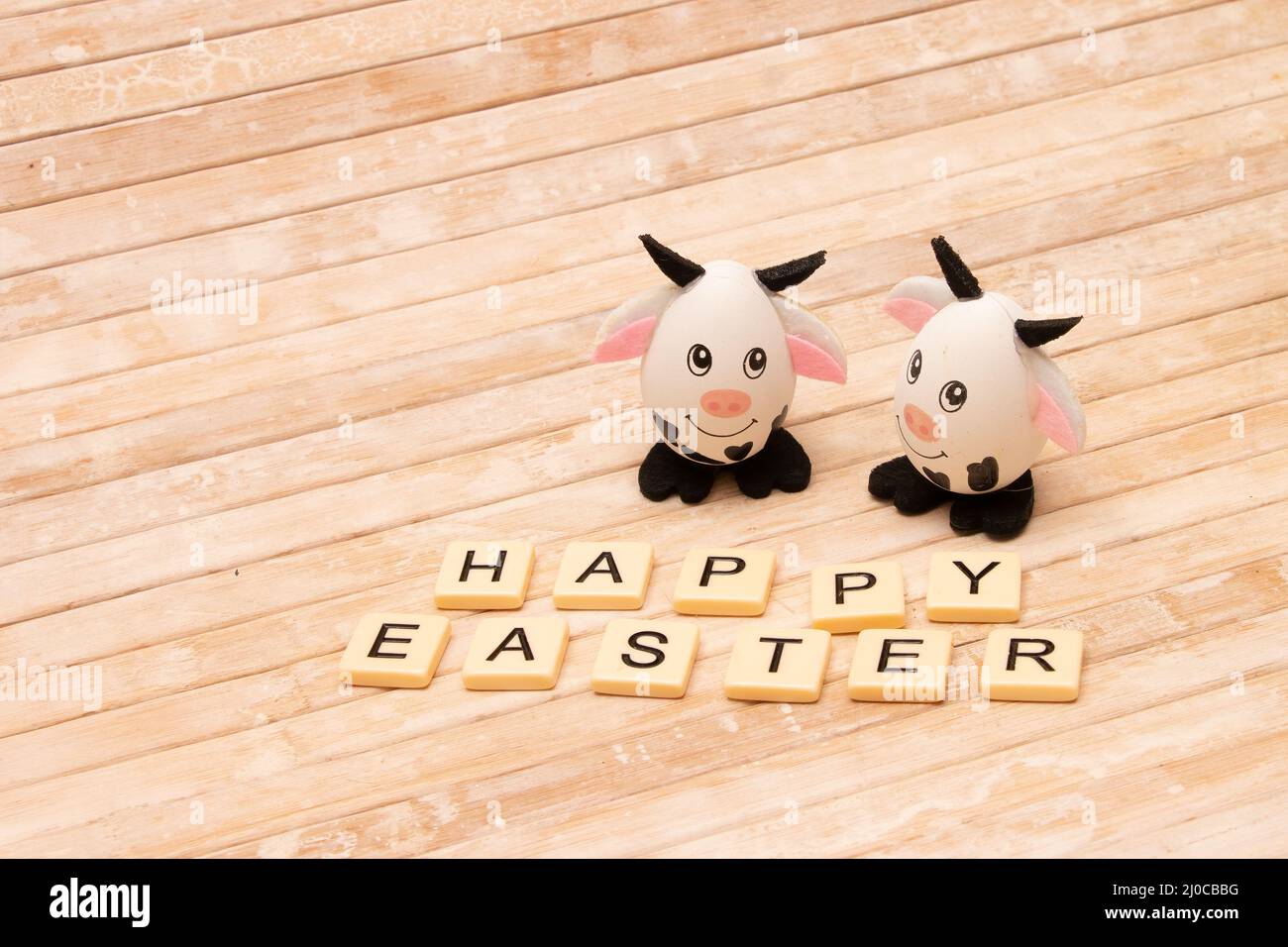 Happy Easter in letter tiles with two egg shaped Cows on wooden ...