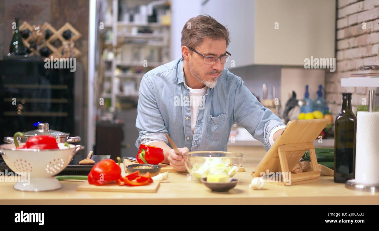 Man cooking in kitchen at home reading recipe on tablet. Healthy eating ...