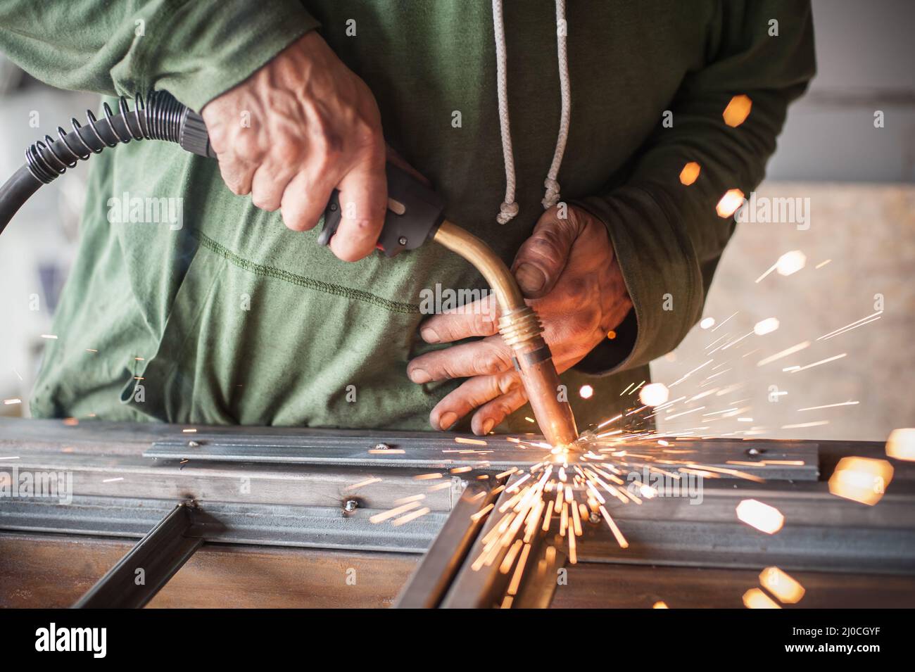 Industrial worker welding the steel structure in the workshop. Flies of spark from hot metal ...