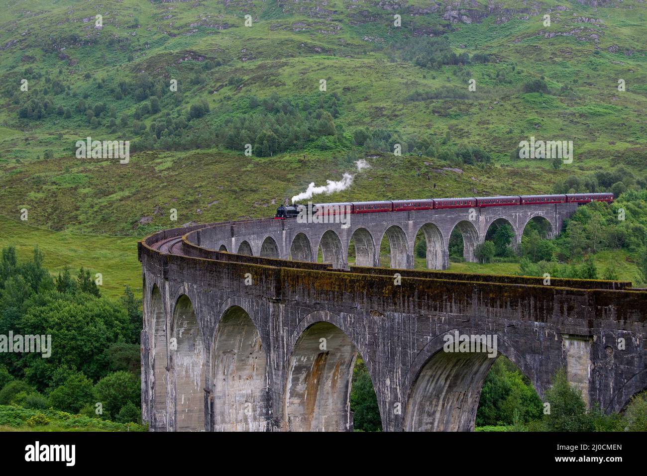 Aerial shot of Jacobite steam train in background of greenery mountains ...