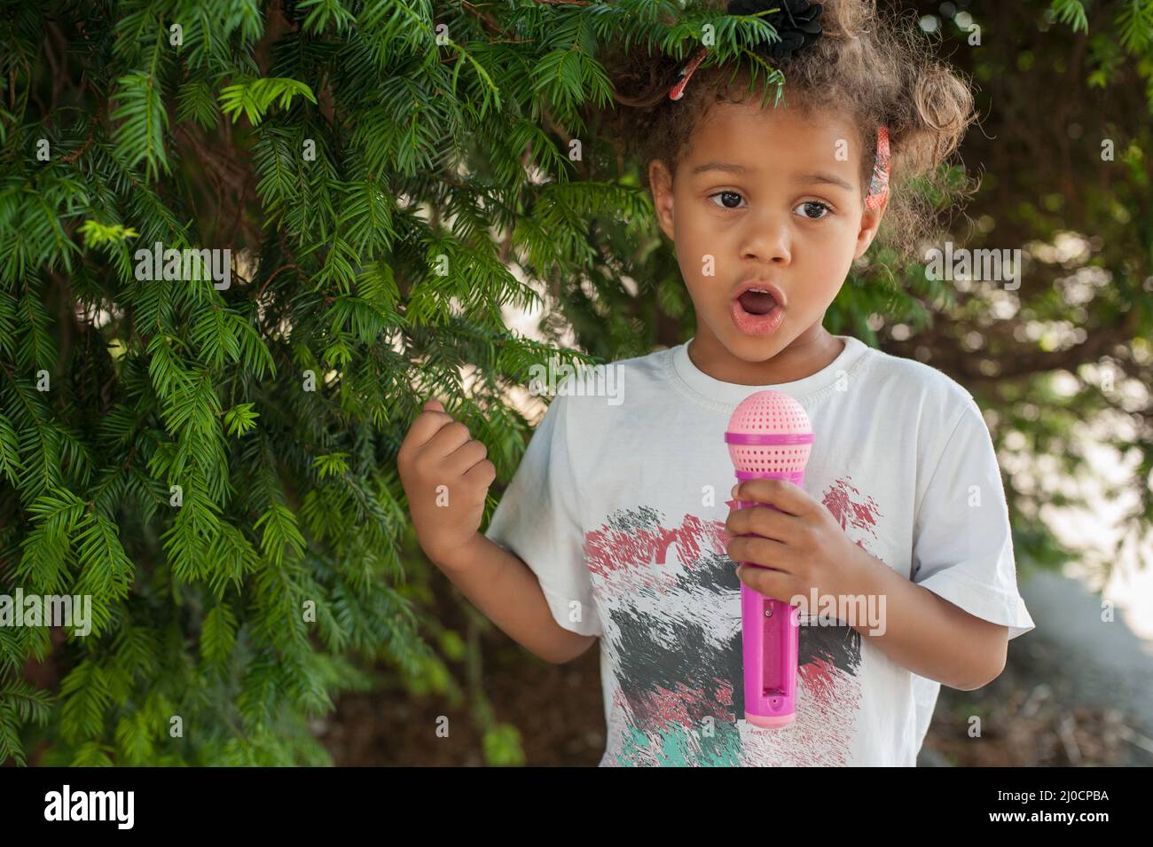 Cute little singer girl singing on the microphone in the city park ...