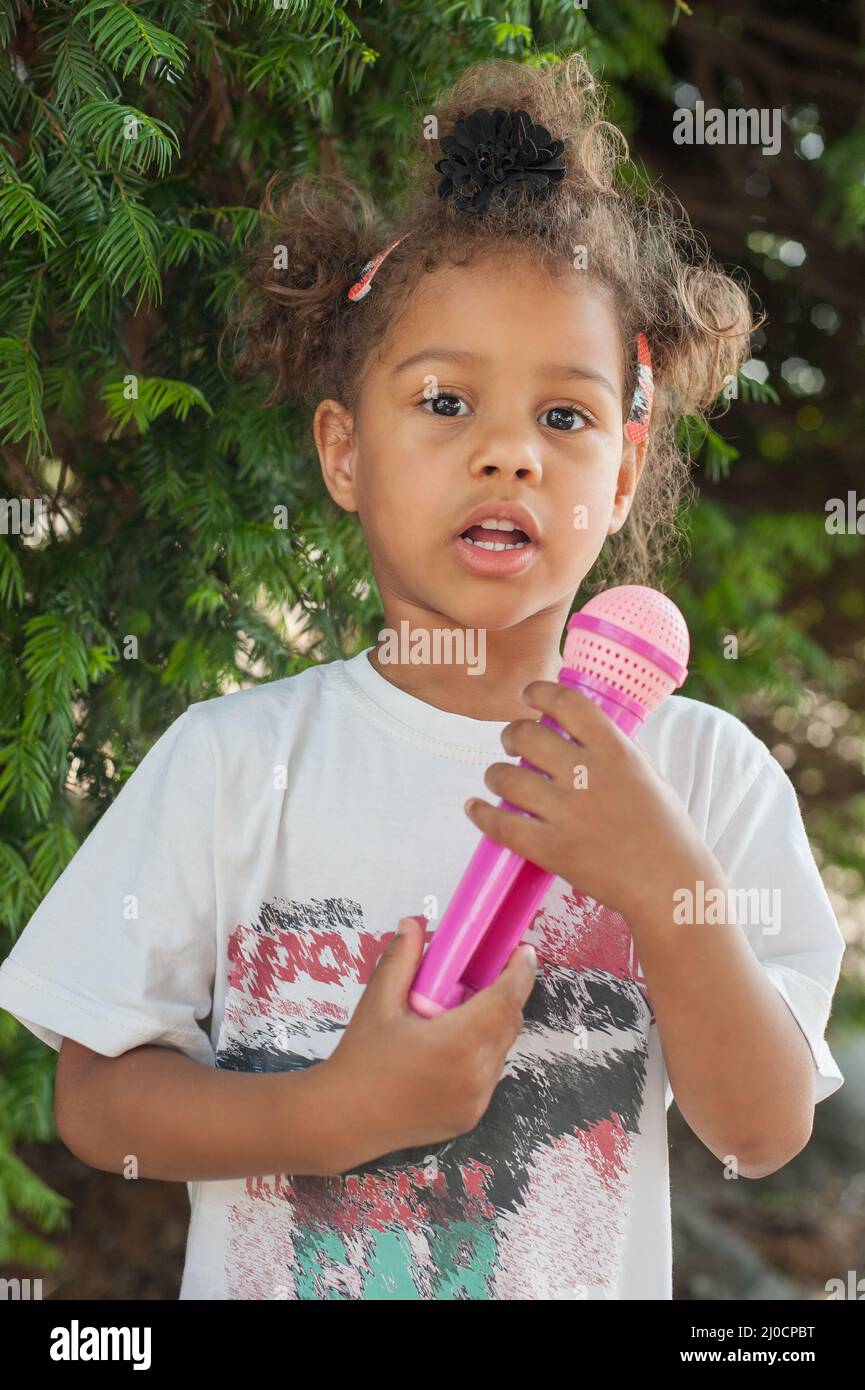 Cute little singer girl singing on the microphone in the city park ...
