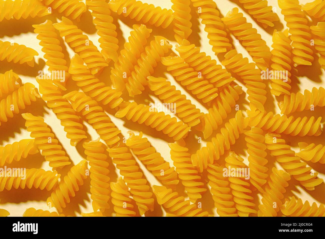 Scattered dried. spiral Italian pasta or noodles on yellow viewed from ...