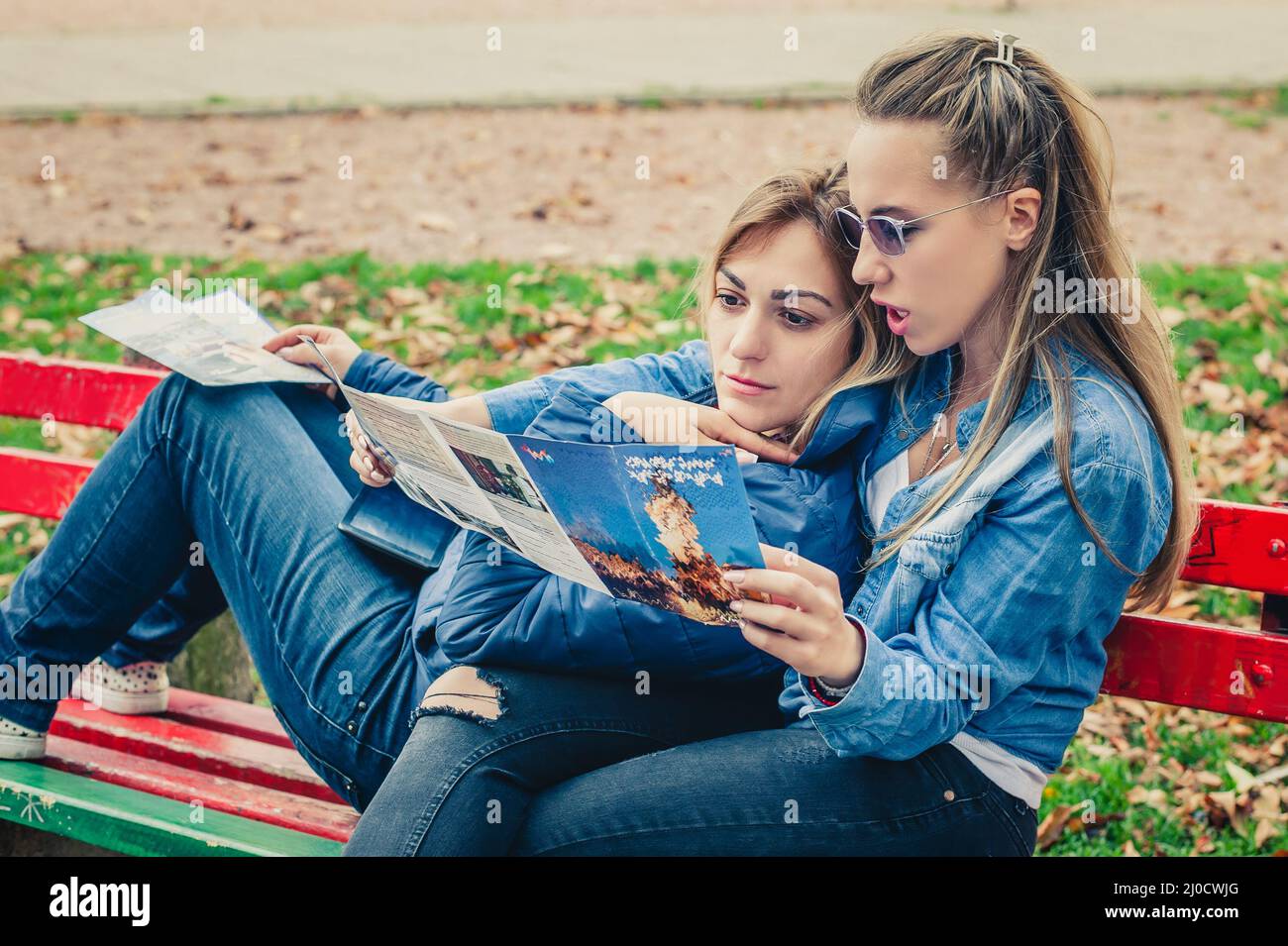 Two women checking the city map, sitting on a bench Stock Photo - Alamy