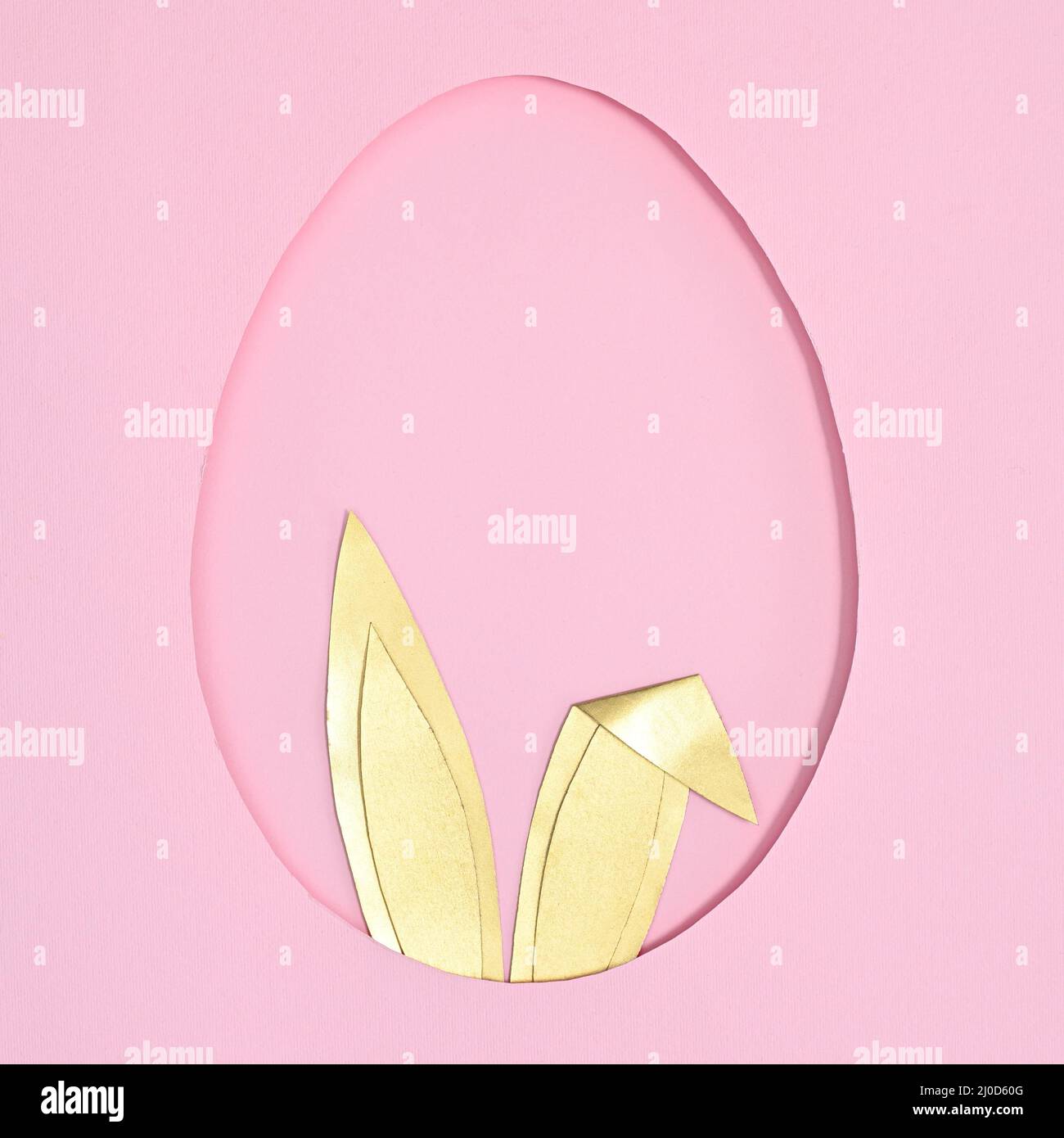 Egg shape frame with golden rabbit ears peek from hole on pastel pink ...