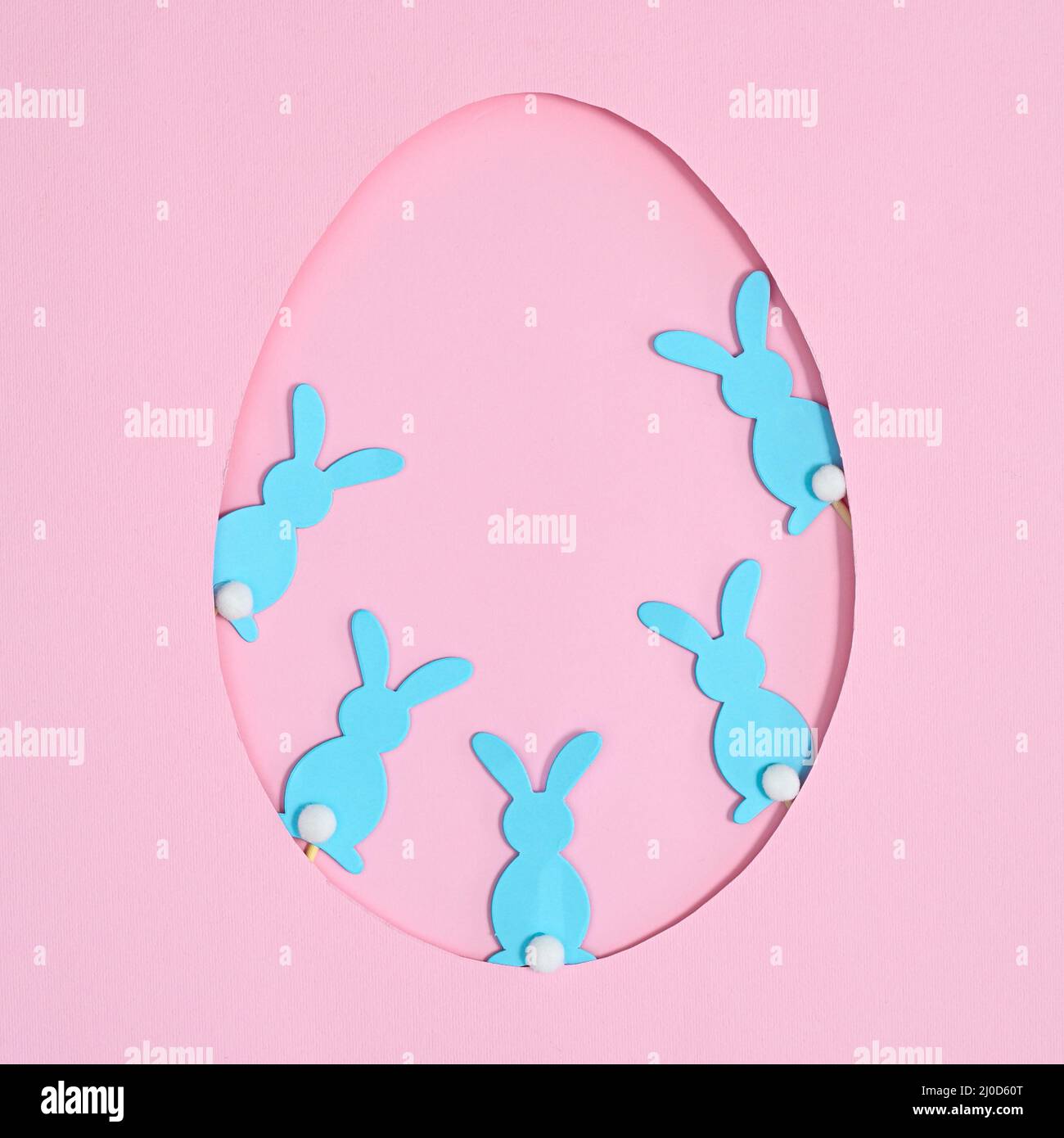 Egg shape frame with blue rabbits on pastel pink background. Flat lay ...