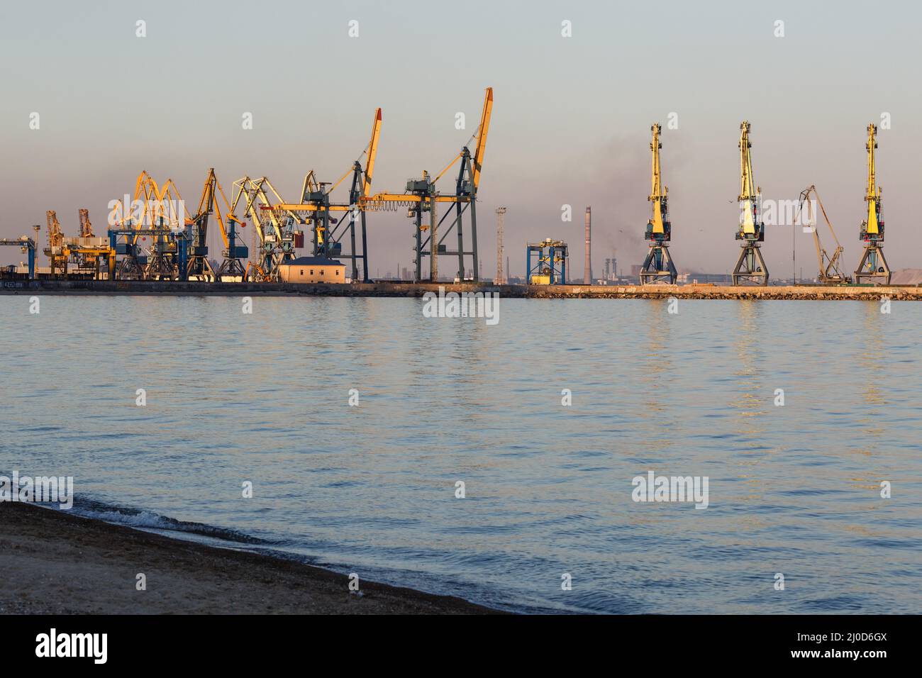 Many big cranes silhouette in the sea port of Azov at golden light of ...