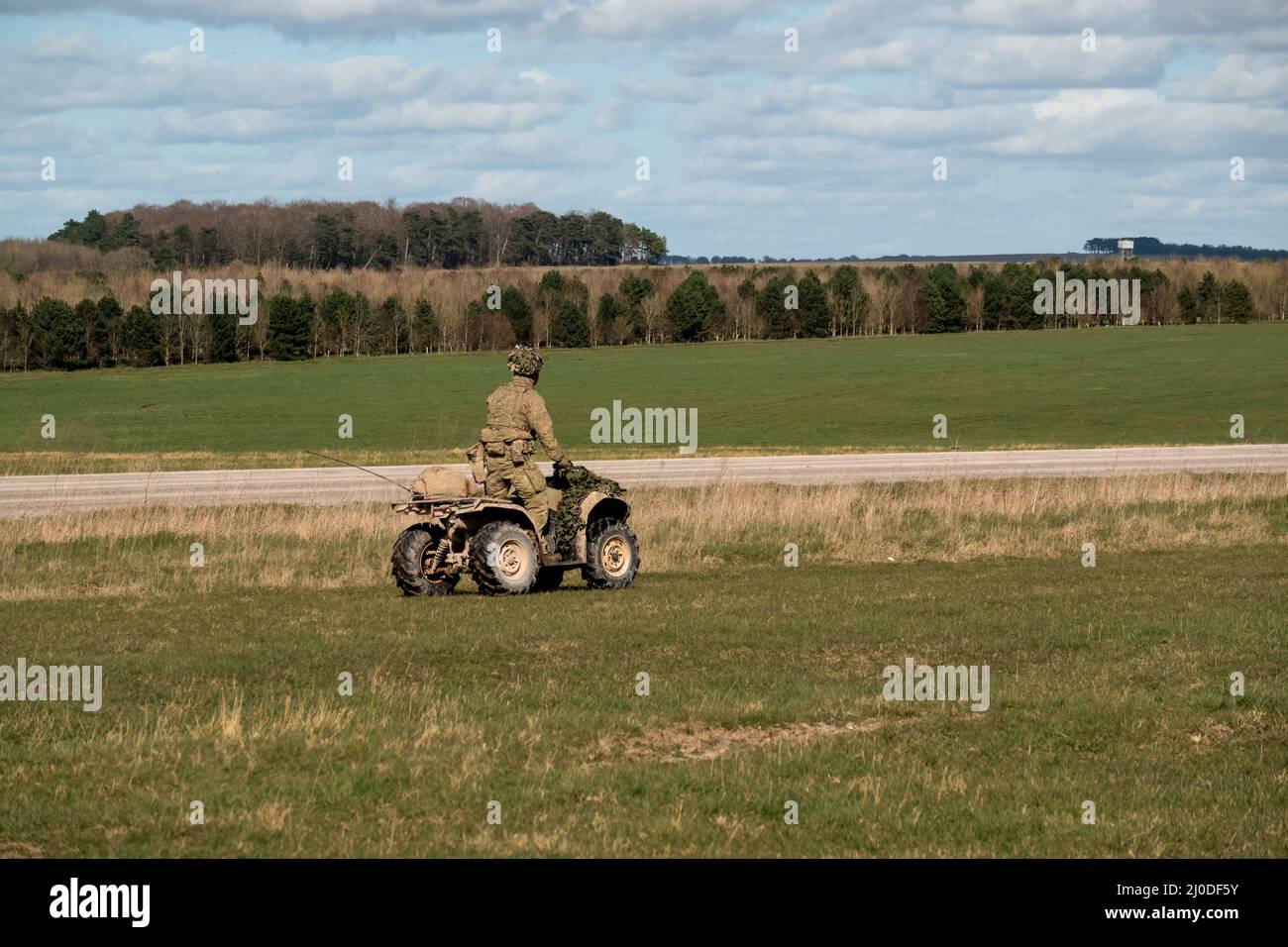 British army soldier driving a small ATV quad bike across open ...