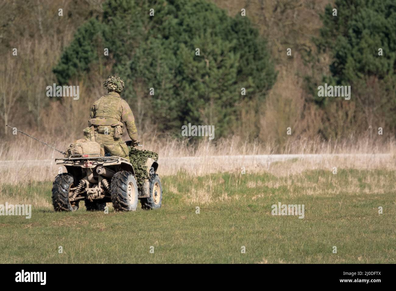 British army soldier driving a small ATV quad bike on a military ...