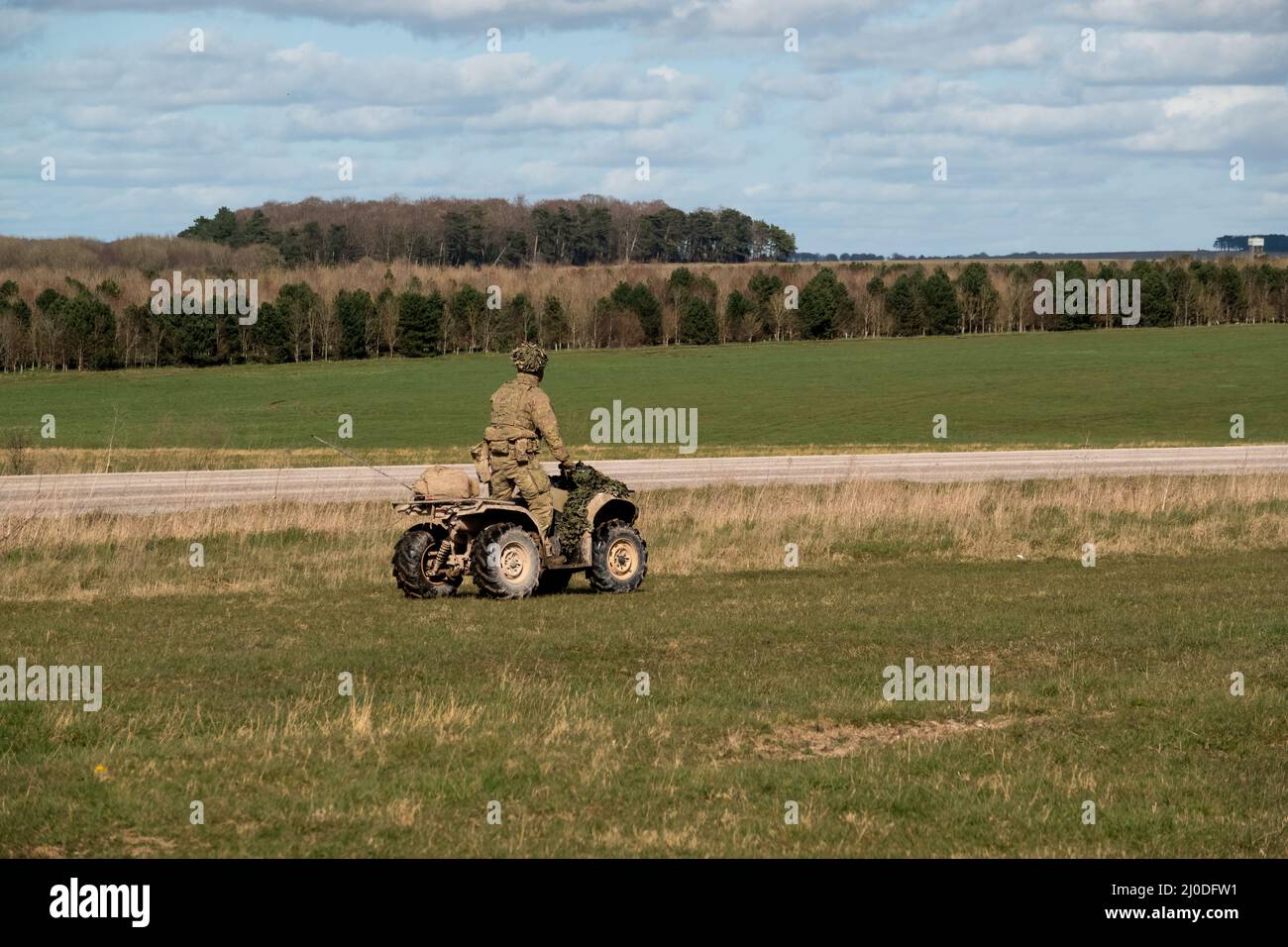 British army soldier driving a small ATV quad bike on a military ...