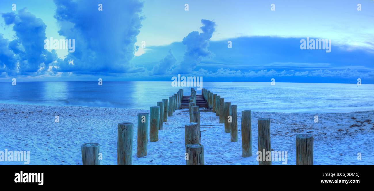 Old pier at dusk at the ocean on Naples Beach with dark skies overhead ...