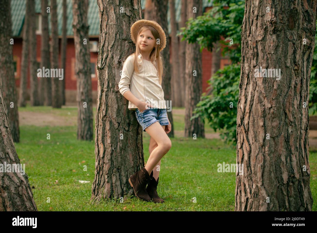 Dreamy preteen girl leaning against tall tree in green courtyard of ...