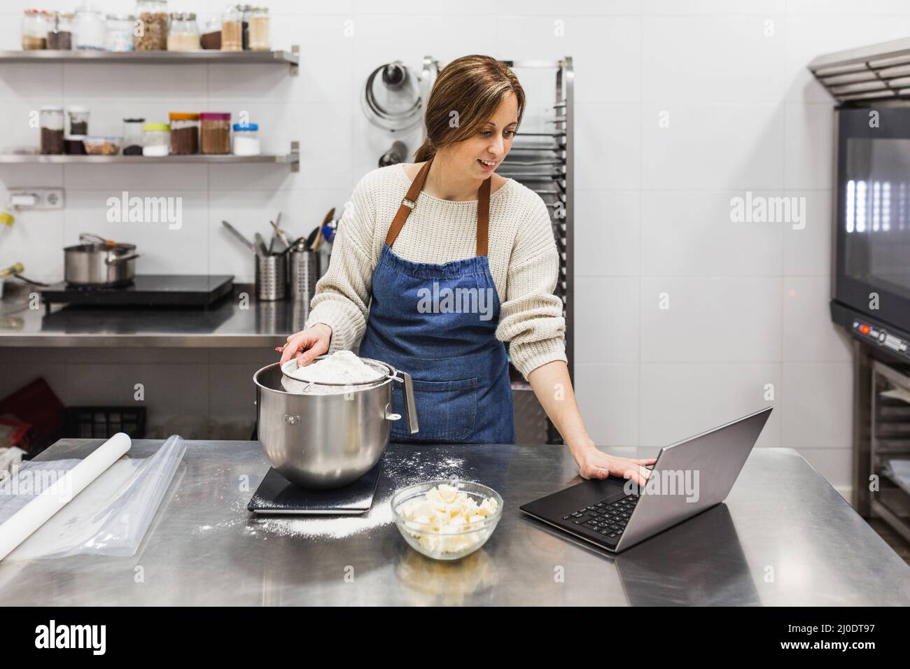 Female pastry chef in an apron following a recipe in the laptop ...