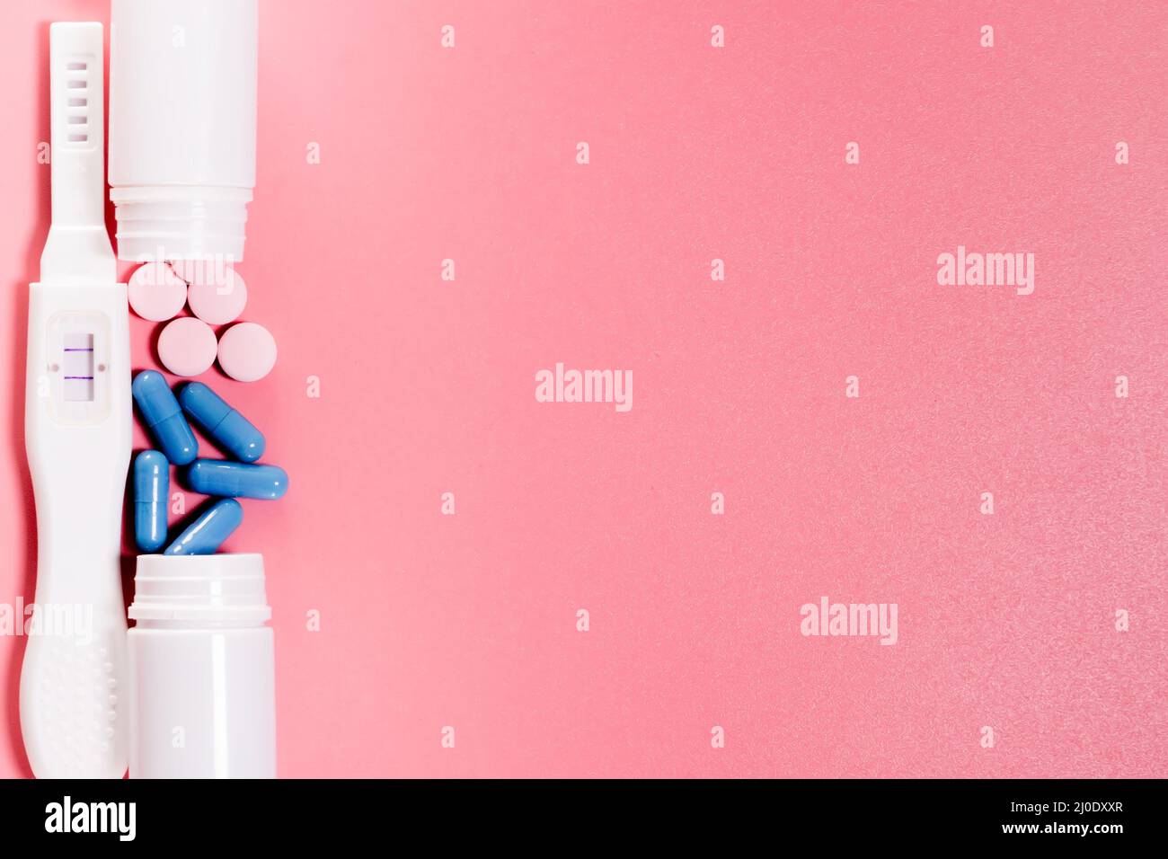 Pregnancy test with two stripes and pink and blue pills. Pastel pink ...