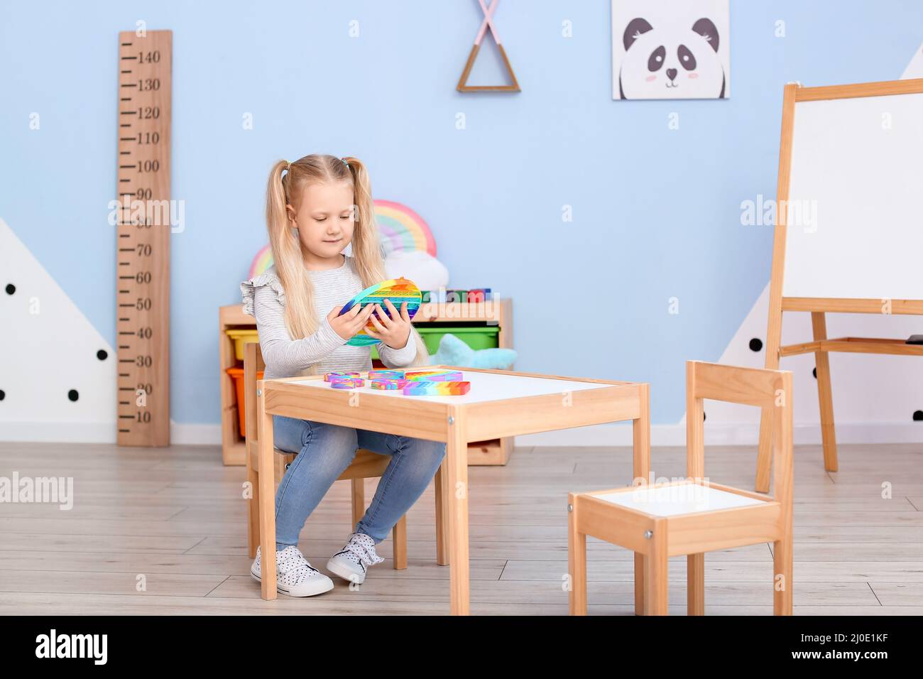 Pretty little girl sitting at table and playing with pop it fidget toy ...