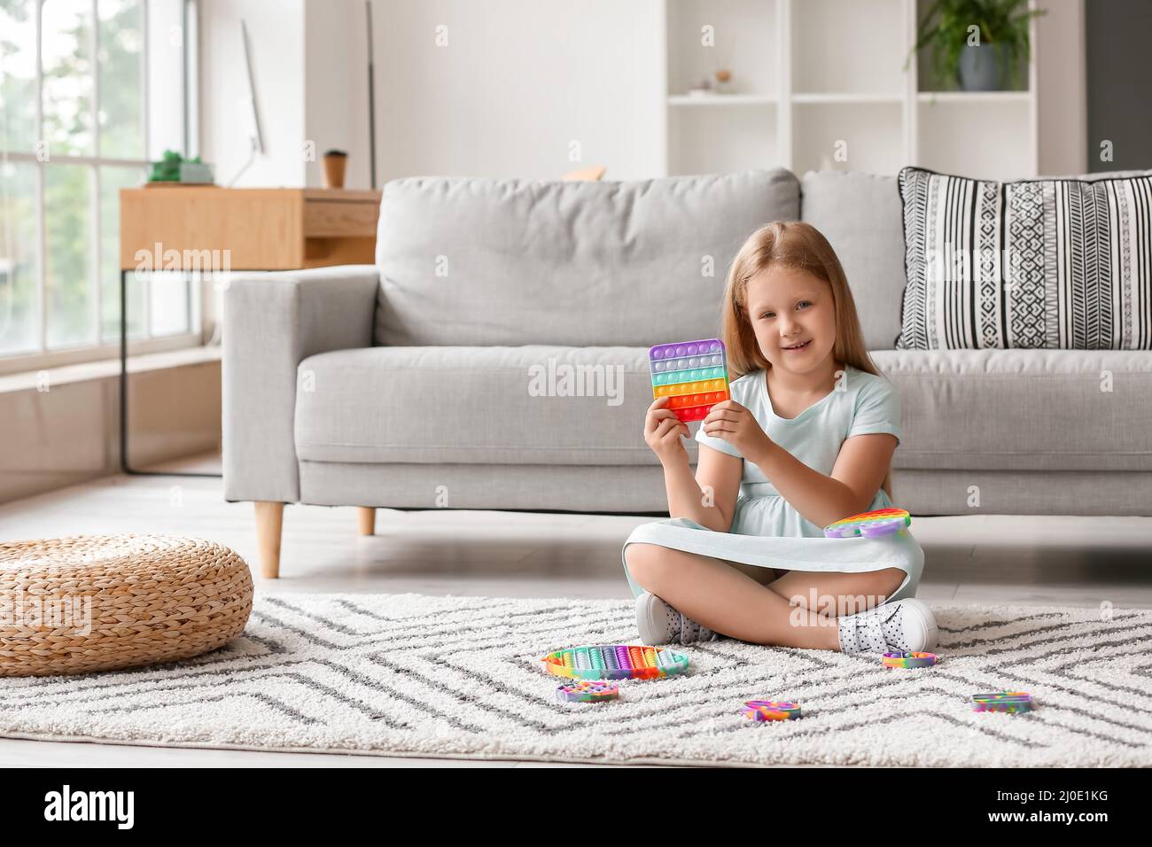 Little girl sitting on floor and holding pop it fidget toy in room ...