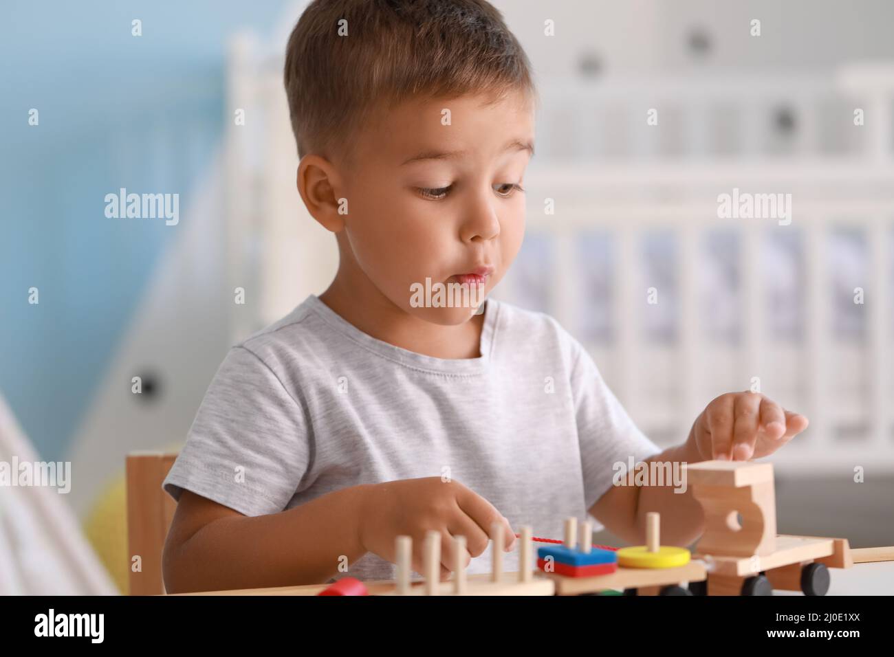 Cute little boy playing with wooden toys at table in room Stock Photo ...