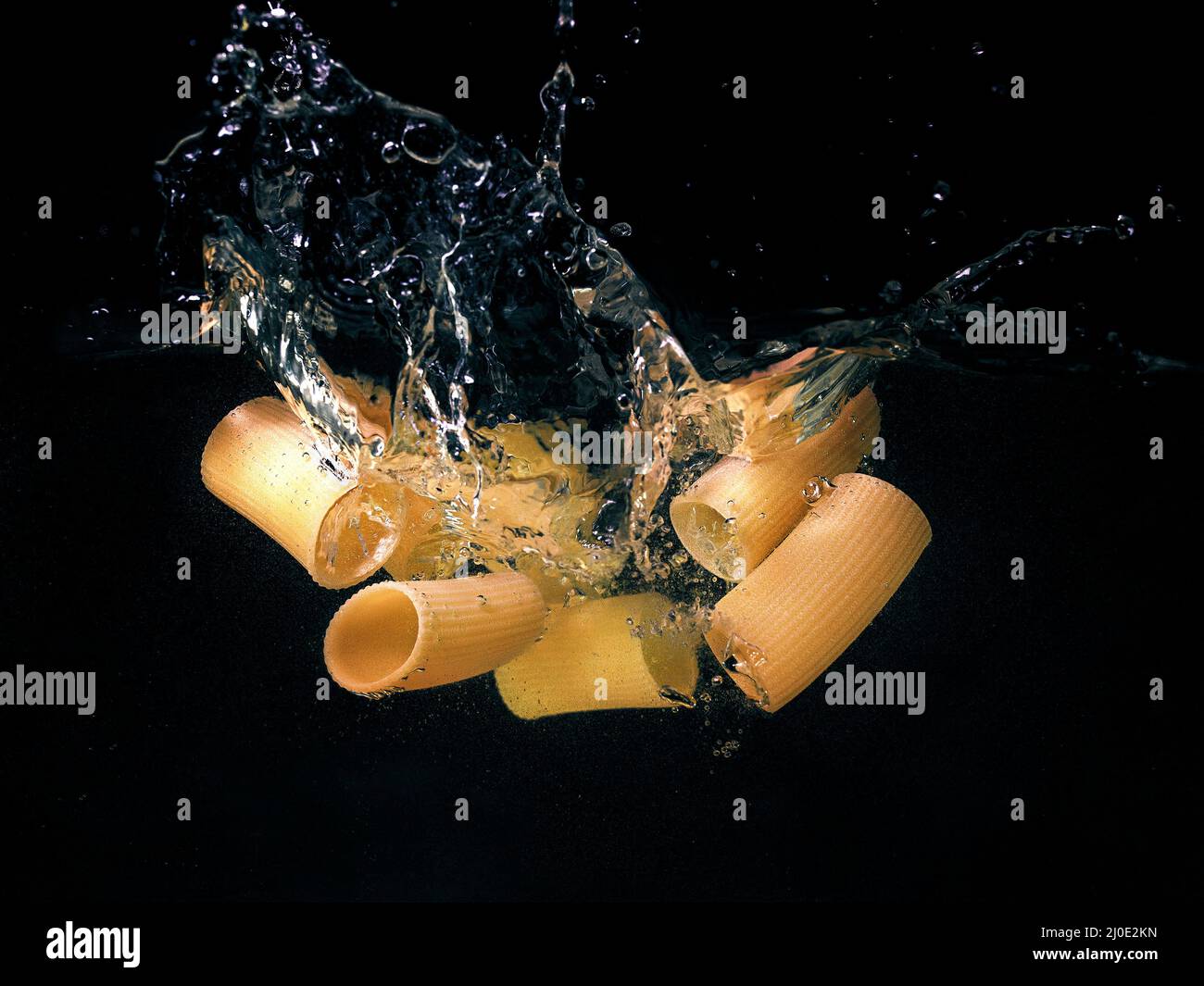 pasta rings falling in the boiling water on dark background. Underwater ...